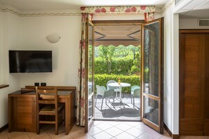 Quarto com mesa e cadeiras de madeira, televisão de tela plana na parede e porta de vidro deslizante para um pátio externo com mesa e cadeiras.