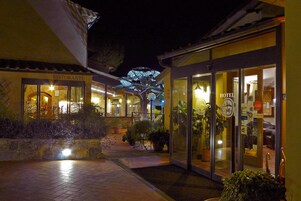 Restaurante e hotel com portas de vidro, plantas em vasos e uma árvore com luzes.