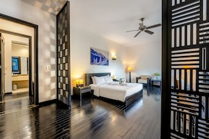 Quarto de hotel moderno com uma cama grande, um ventilador de teto, uma mesa de cabeceira com abajur e uma imagem pendurada na parede.