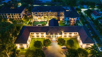 Vista aérea de um grande hotel com vários andares, um pátio central, vegetação exuberante e uma piscina.