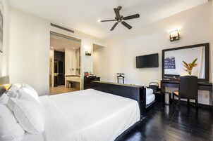 Quarto de hotel com cama, escrivaninha, cadeira, televisão e ventoinha no teto.