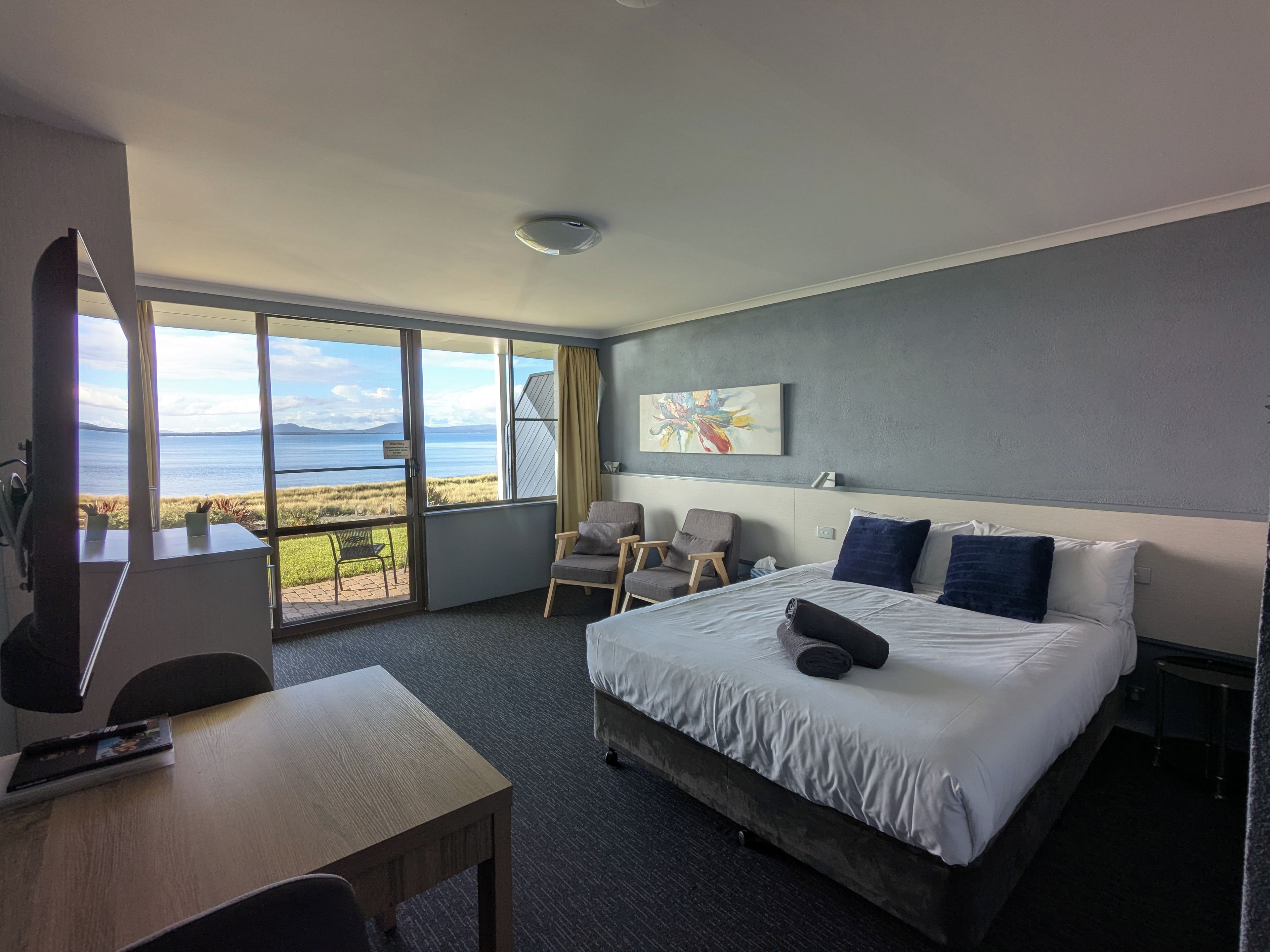 Quarto de hotel com cama, escrivaninha, cadeira e vista para o mar.