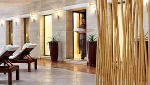 Um saguão de hotel com poltronas de madeira, plantas grandes em vasos e uma área de recepção com uma pessoa segurando um objeto branco.