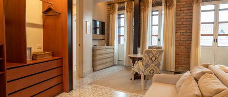 Quarto de hotel com guarda-roupa de madeira, sofá, mesa pequena, televisão e janela com cortinas.