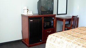 Quarto de hotel com uma cama, escrivaninha de madeira, televisão, micro-ondas e frigorífico.
