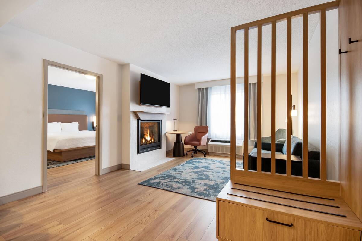 Quarto de hotel com uma cama, televisão, lareira, escrivaninha e uma cadeira.