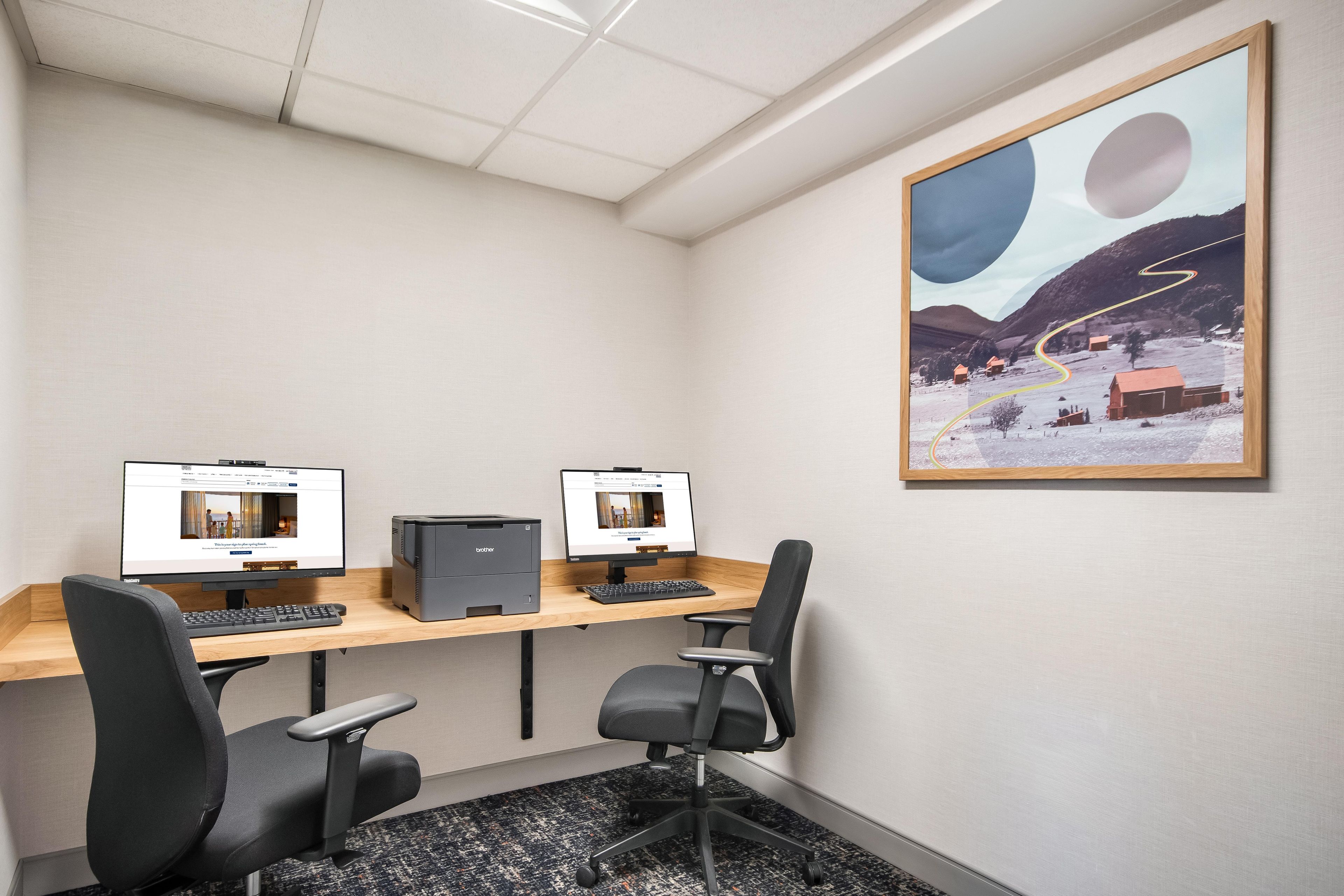 Um espaço de trabalho com dois computadores de mesa, uma impressora e cadeiras de escritório.