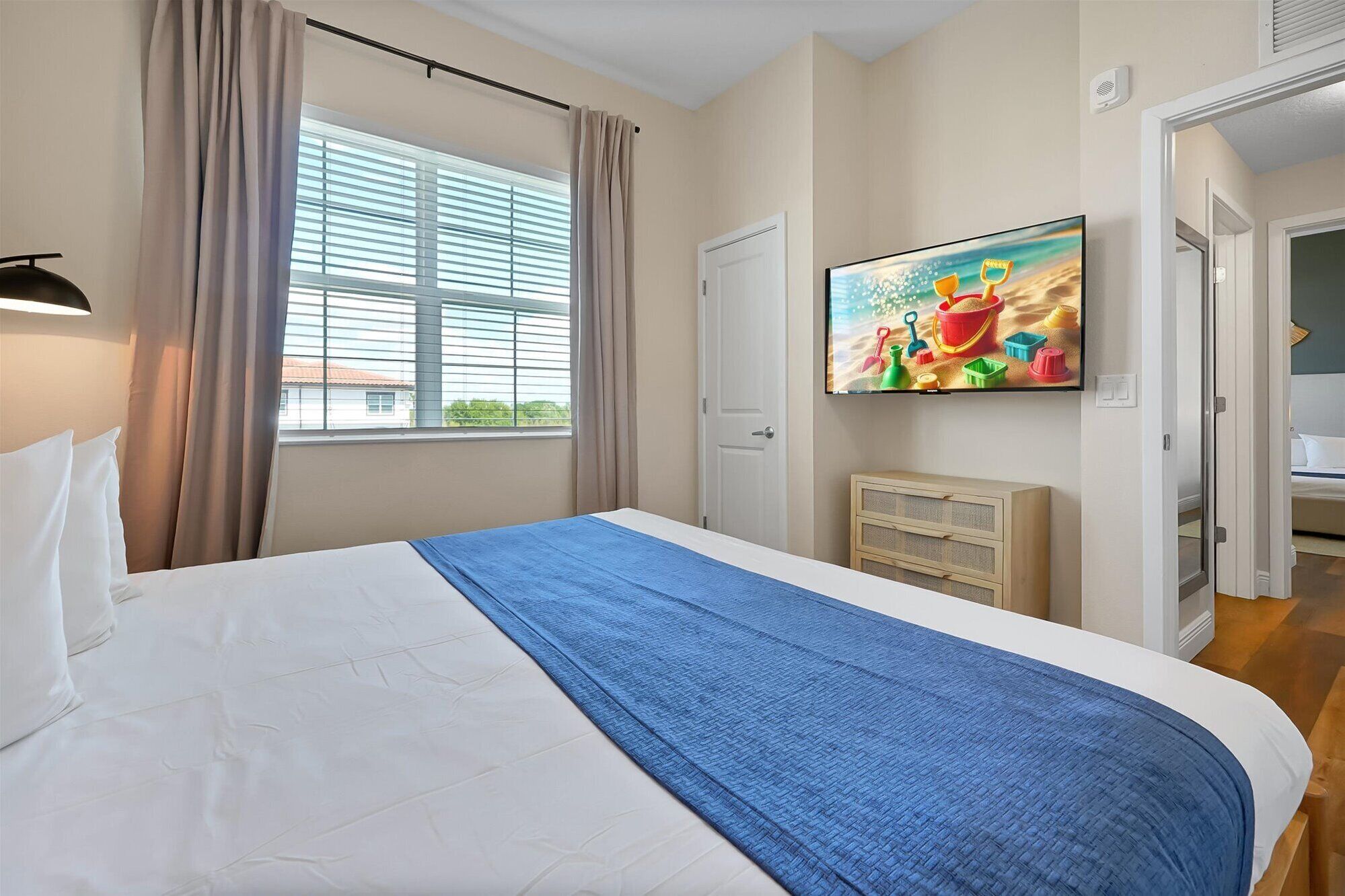 Quarto de hotel com cama, televisão na parede, janela com cortinas e porta.