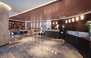 Uma área de recepção moderna com piso de mármore, balcão de atendimento e espaço de espera com cadeiras.