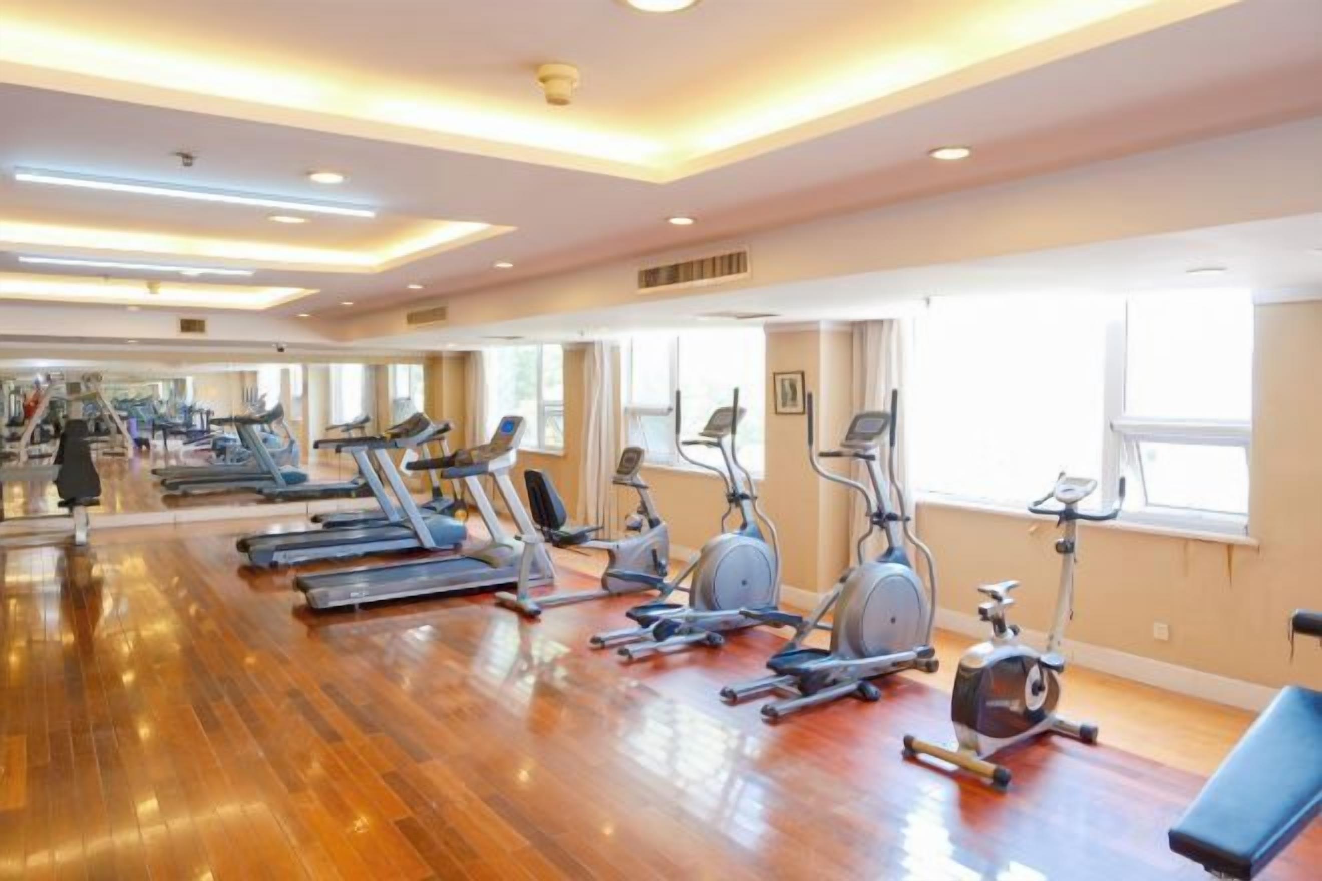 Uma academia com diversos equipamentos de ginástica, amplas janelas e piso de madeira.