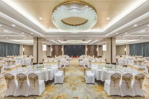 Salão de banquetes com mesas redondas, toalhas brancas e fitas douradas.