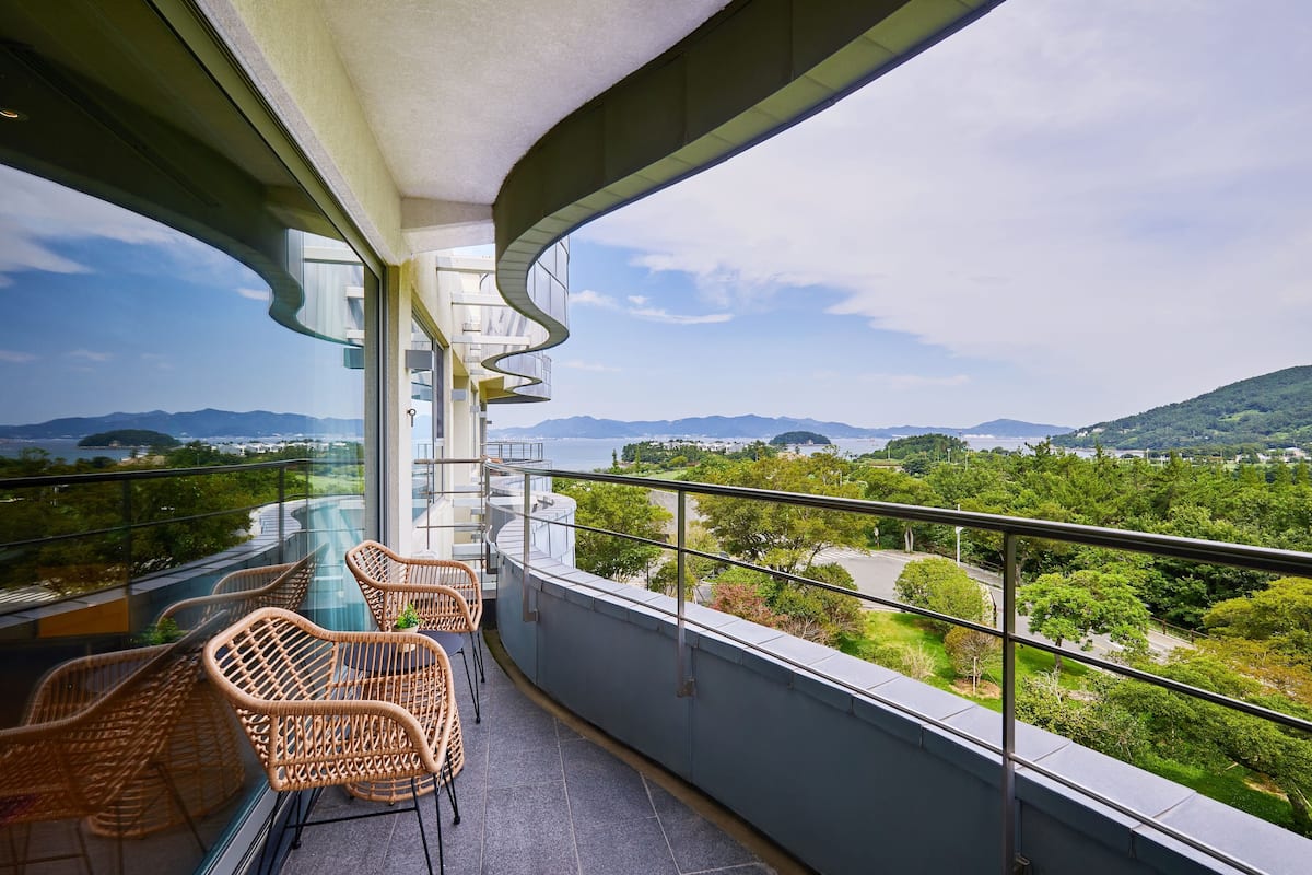 Varanda com cadeiras de vime e uma mesa de vidro, com vista para um horizonte urbano e montanhas ao longe.