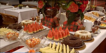 Uma mesa de buffet com diversos alimentos, incluindo fatias de melancia, um bolo de chocolate e outras sobremesas.