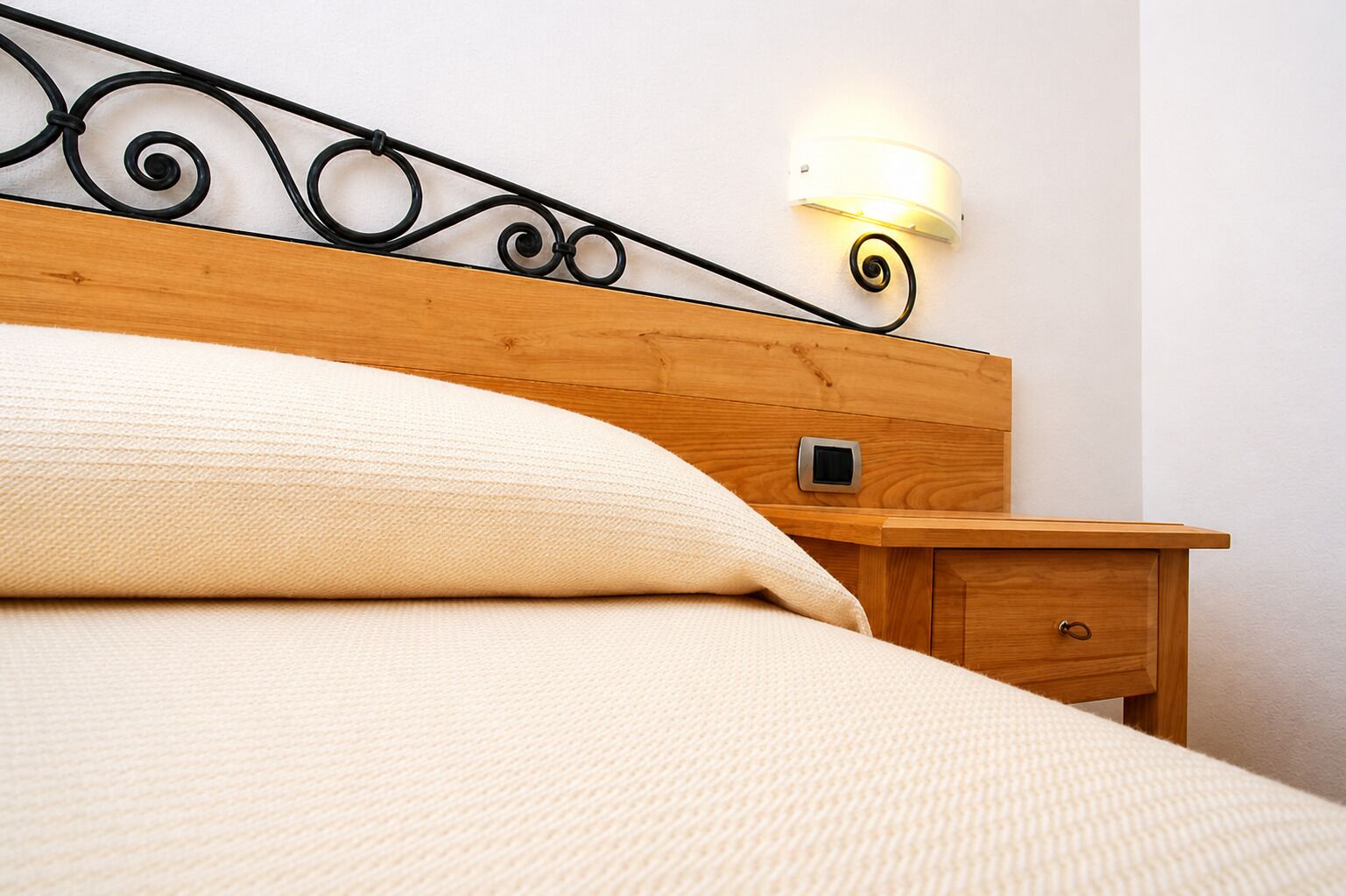 Uma cama com cabeceira de madeira, uma mesa de cabeceira com abajur e uma gavetinha.