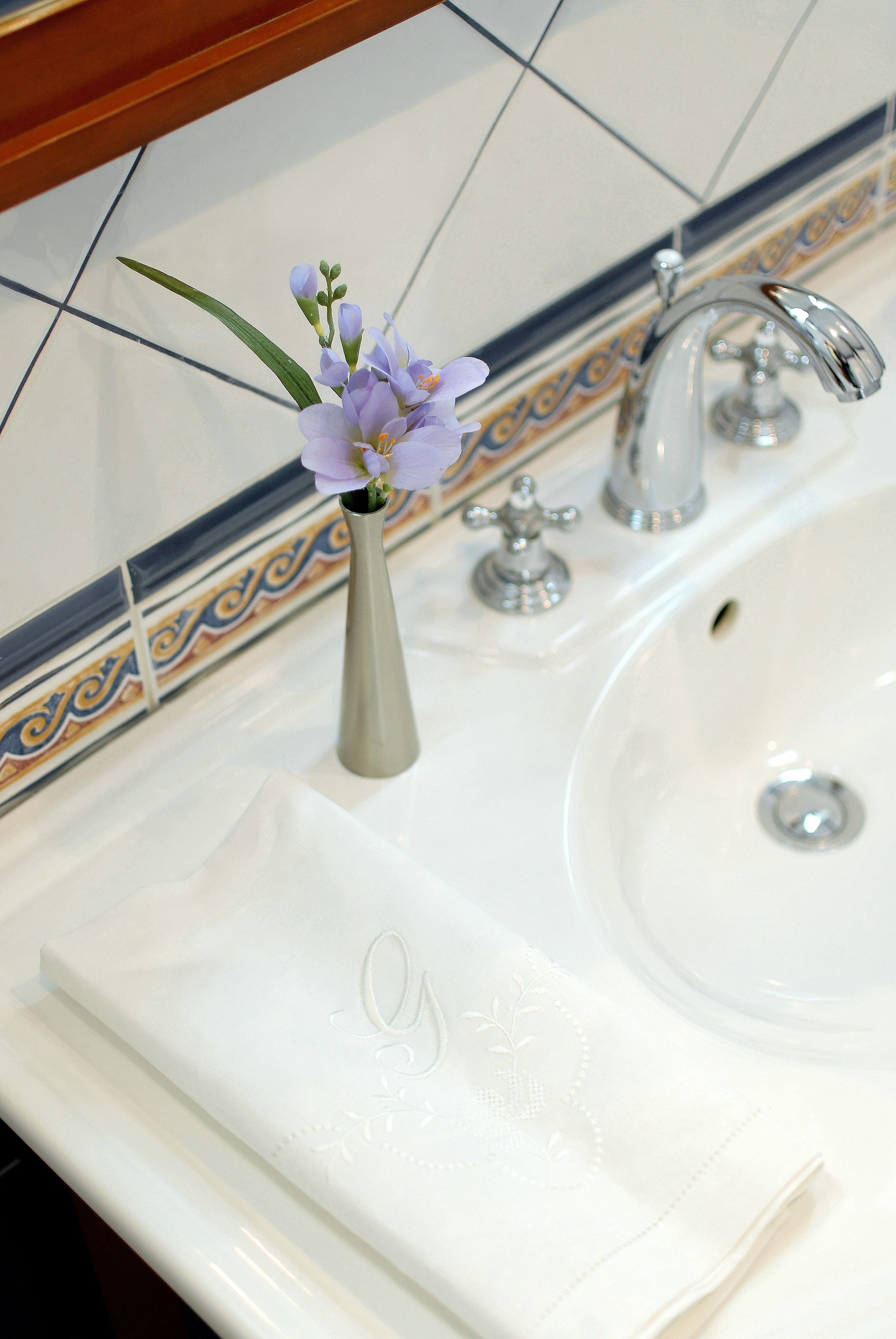 Uma pia de banheiro com um vaso de flores, uma toalha e um espelho com azulejos decorativos.