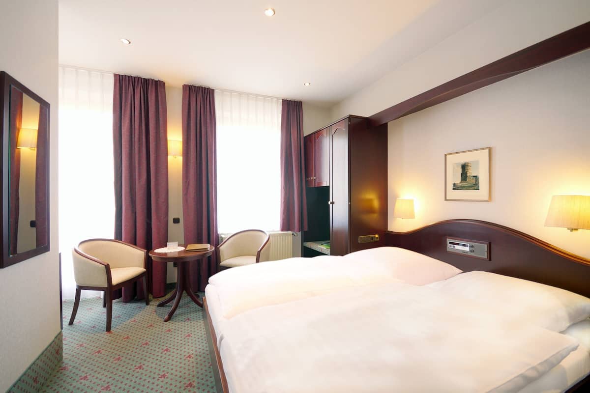 Quarto de hotel com uma cama grande, duas cadeiras, uma mesa pequena e uma escrivaninha.