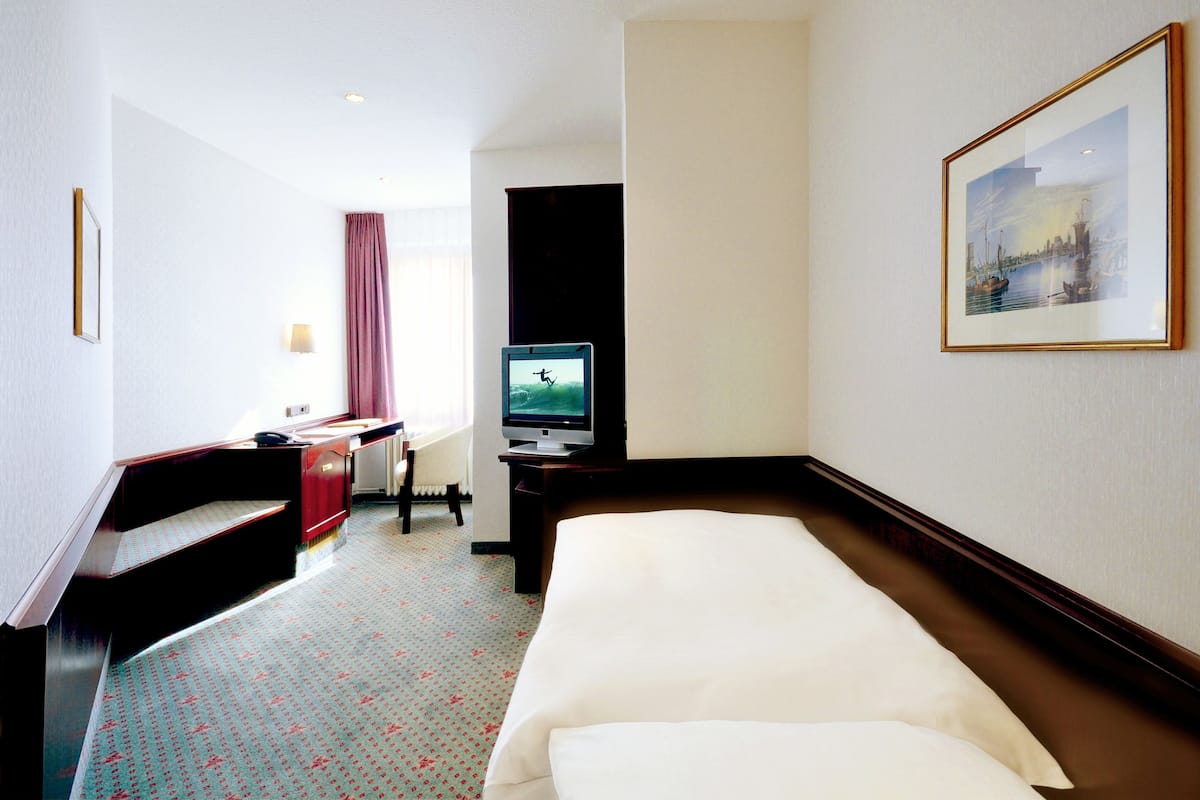 Quarto de hotel com uma cama, escrivaninha, televisão e um quadro na parede.