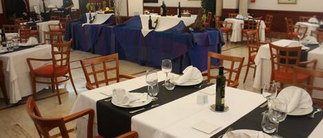 Restaurante com mesas montadas para refeições, cadeiras e um garçom ao fundo.