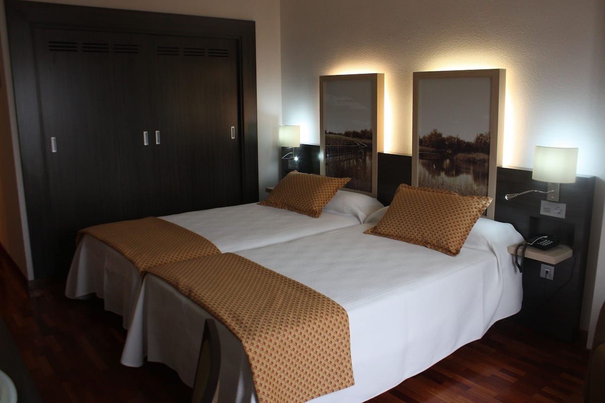 Quarto de hotel com duas camas, um guarda-roupa, luminárias e um telefone.