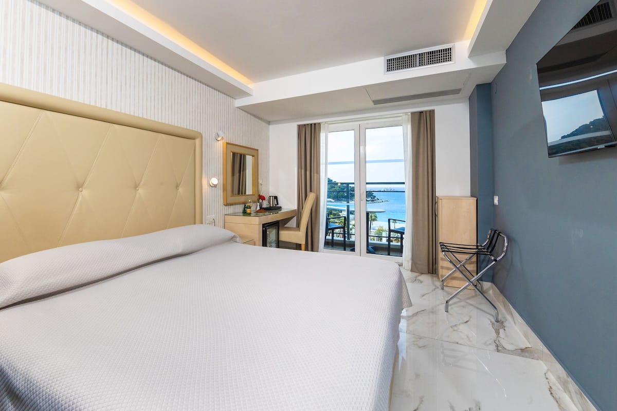Quarto de hotel com uma cama grande, uma mesa, uma cadeira, uma televisão e vista para o mar.