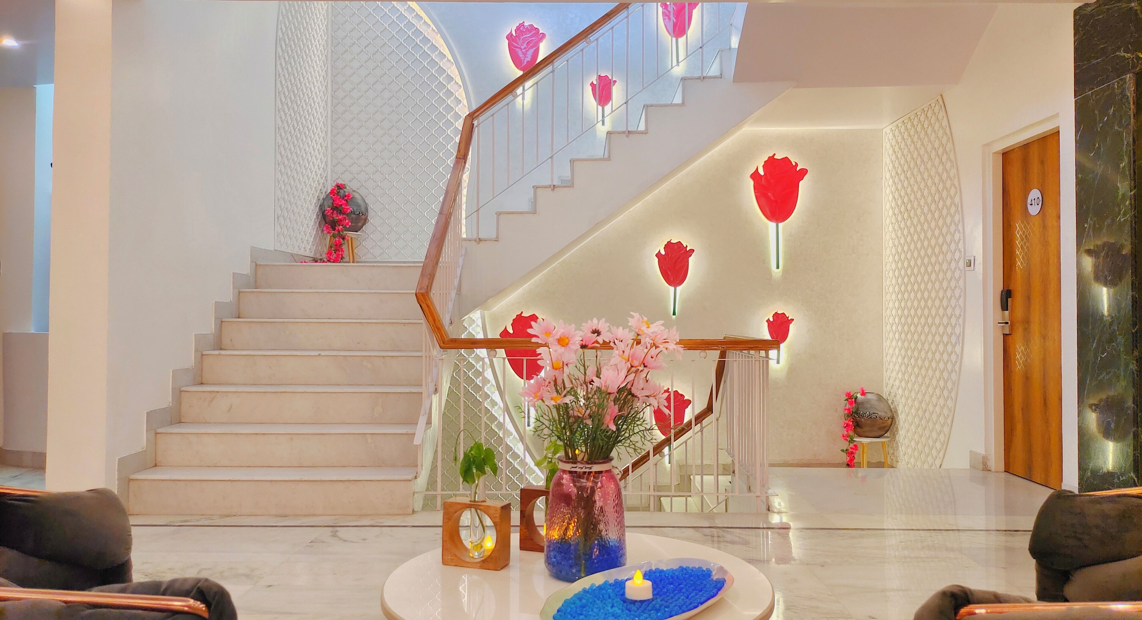 Um hall de hotel moderno com uma escadaria de mármore, um balcão de recepção e um vaso decorativo com flores.