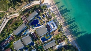Vista aérea de um resort com várias piscinas, uma praia e palmeiras.