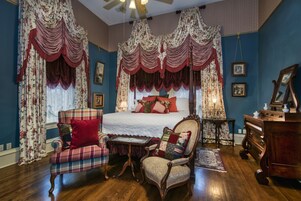 Quarto com cama, duas cadeiras, cômoda e espelho.