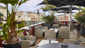 Terraço no telhado com móveis de vime, plantas em vasos e guarda-sóis para sombra.