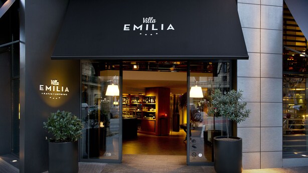Exterior da Villa Emilia, com fachada moderna, grandes vasos de plantas e uma entrada acolhedora.