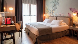 Quarto de hotel com uma cama grande, uma escrivaninha com abajur, uma cadeira e um quadro na parede.