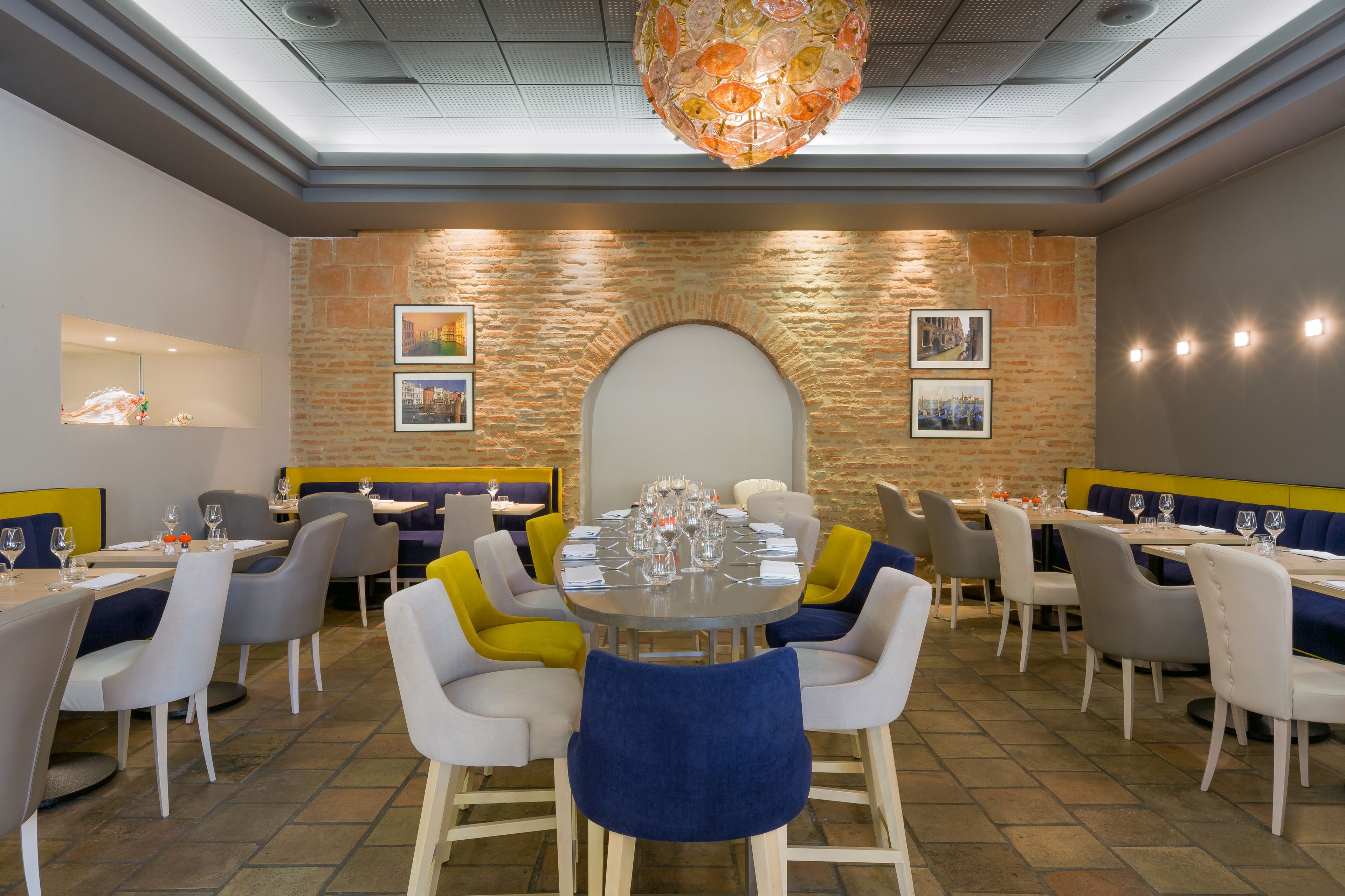Um restaurante com mesas redondas, cadeiras brancas e azuis e uma parede de pedra com quadros.