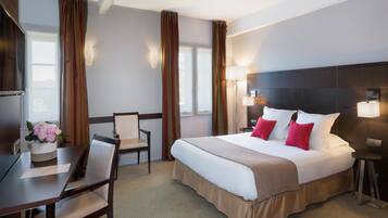 Quarto de hotel com uma cama grande, uma escrivaninha, uma cadeira e uma mesinha.