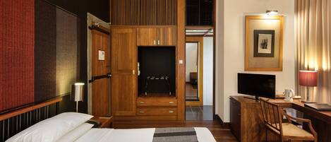 Quarto de hotel com cama, escrivaninha com televisão, uma cadeira e guarda-roupa.