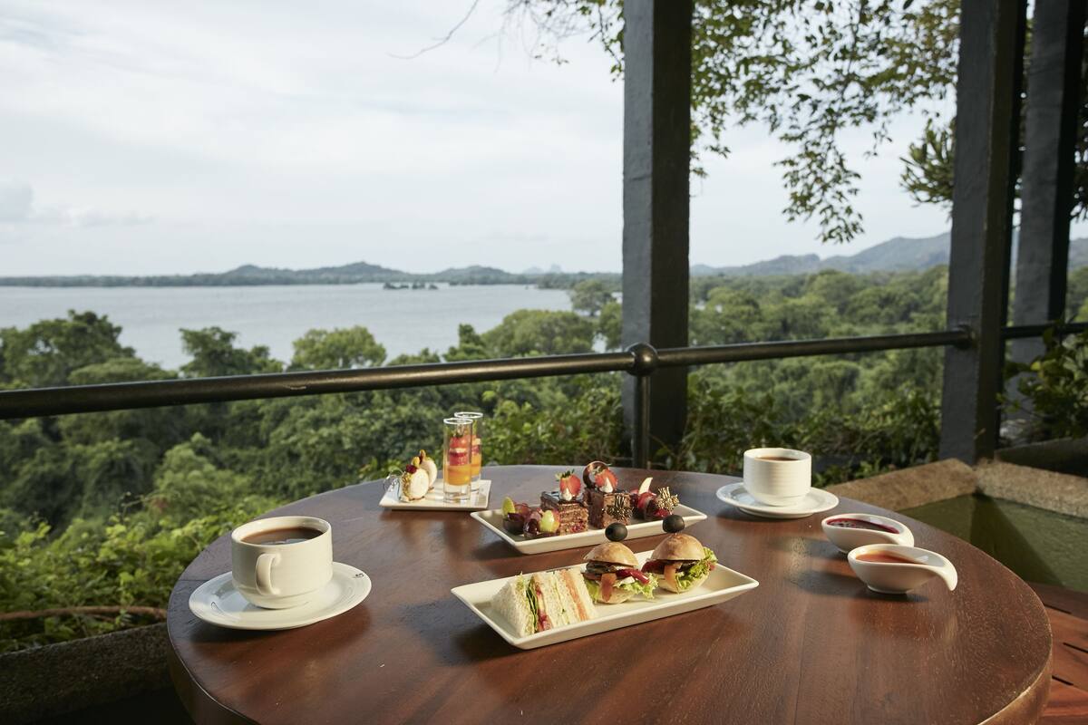 Uma mesa com comida e bebidas, com vista para a água e vegetação.
