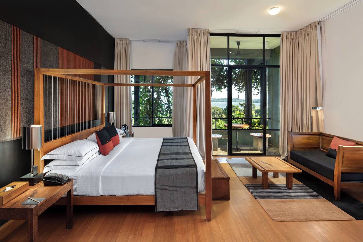 Quarto moderno com cama de dossel, escrivaninha de madeira, sofá e varanda com mesa.