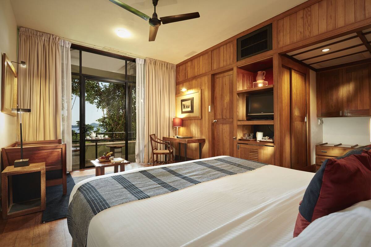 Quarto de hotel com uma cama grande, uma escrivaninha, uma cadeira e vista para o exterior.