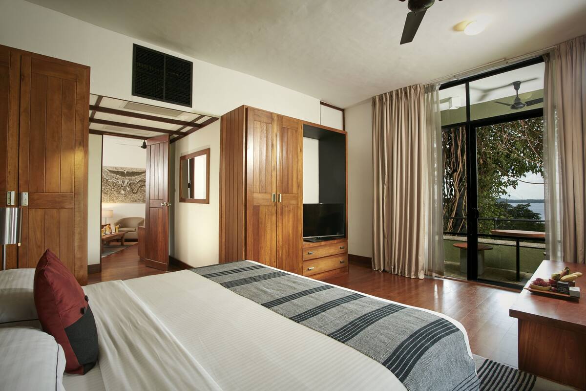 Quarto com cama grande, guarda-roupa de madeira, TV e varanda com vista.