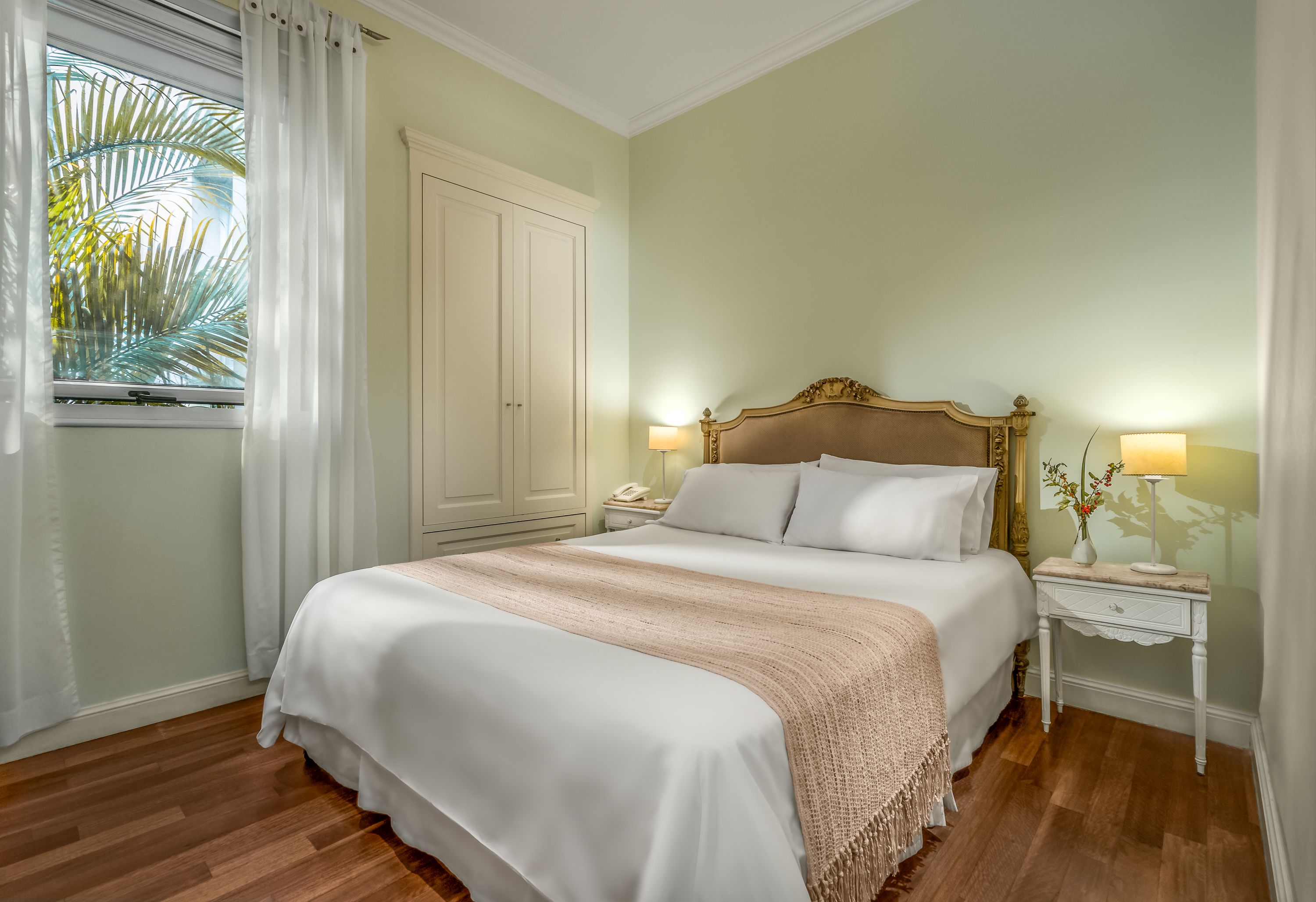 Quarto bem organizado com uma cama grande, mesa de cabeceira com abajur e janela com cortinas.