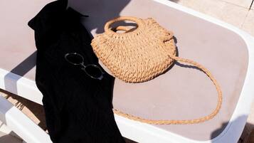 Uma espreguiçadeira branca com uma bolsa trançada e roupas pretas sobre ela.