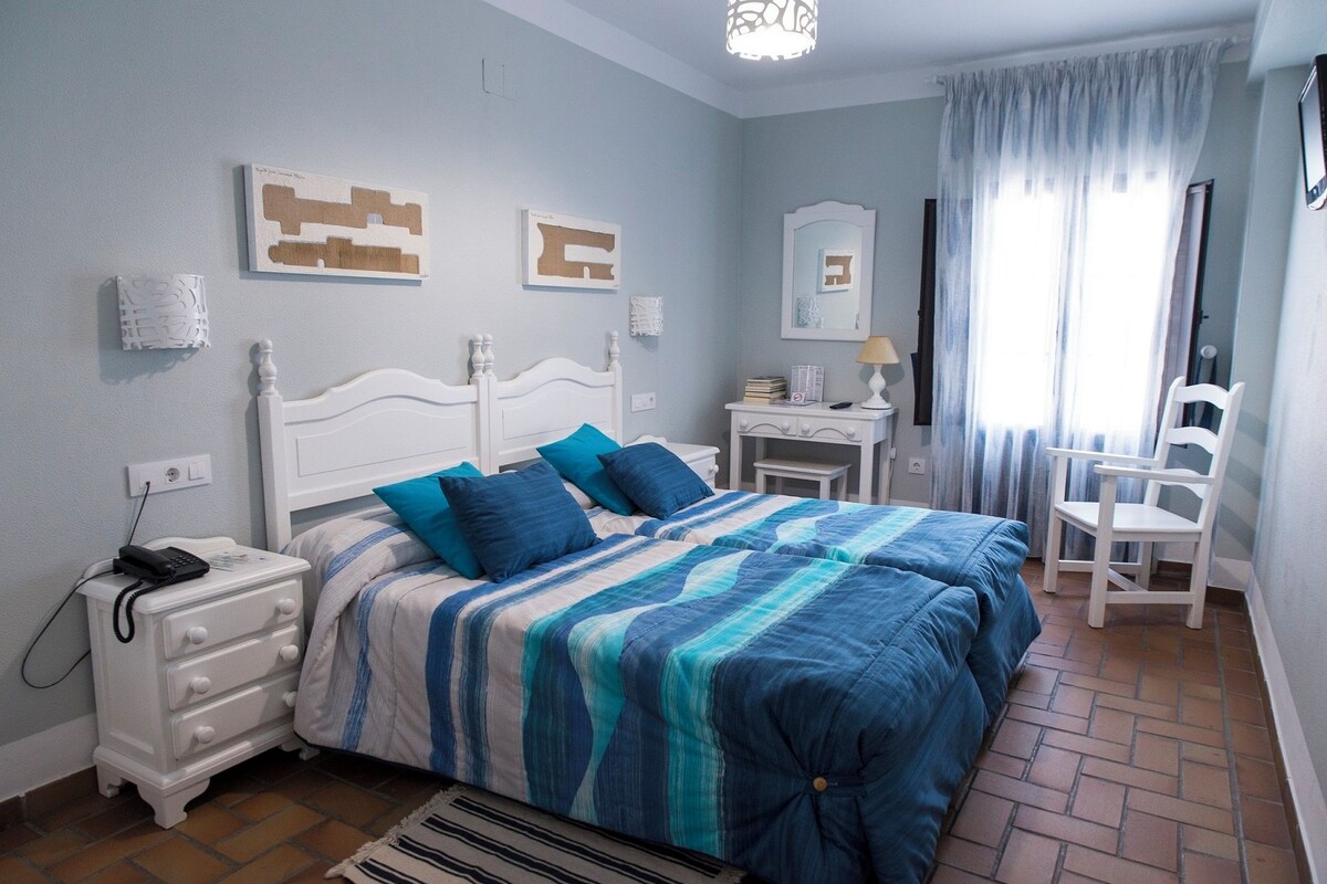 Um quarto com cama, mesas de cabeceira, escrivaninha e uma cadeira.