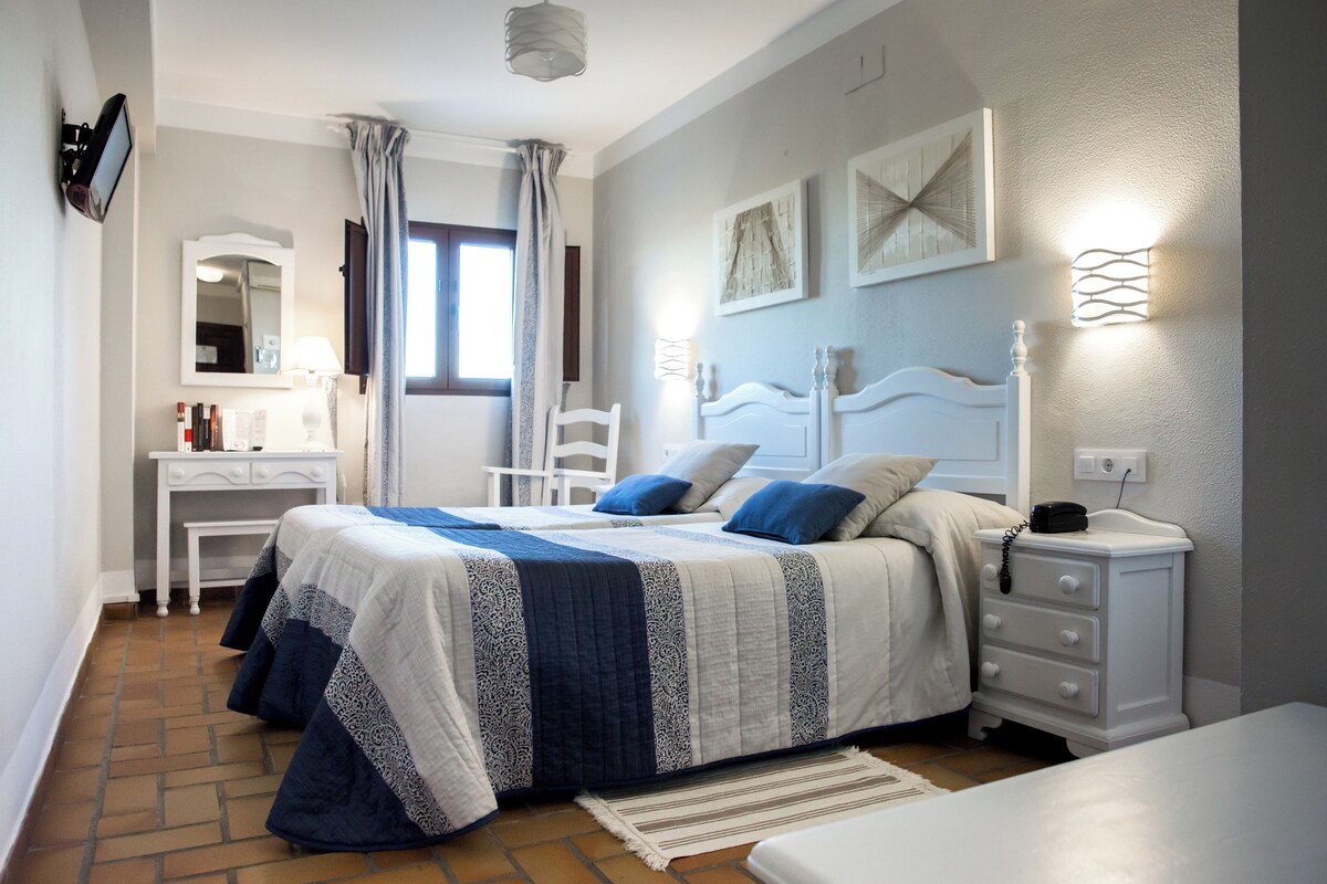 Um quarto com cama, mesa de cabeceira, escrivaninha e uma secretária com cadeira.