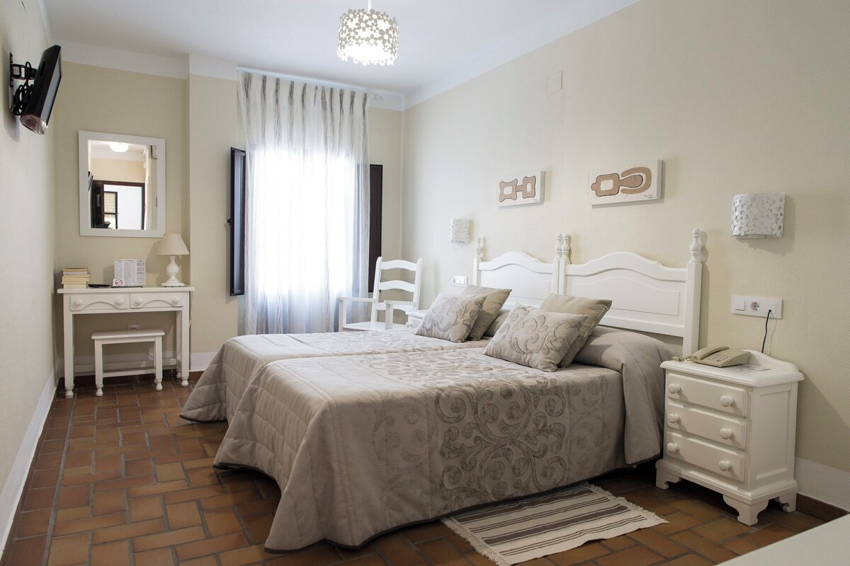 Quarto com cama de casal, mesas de cabeceira, escrivaninha, cadeira e luminária pendente.