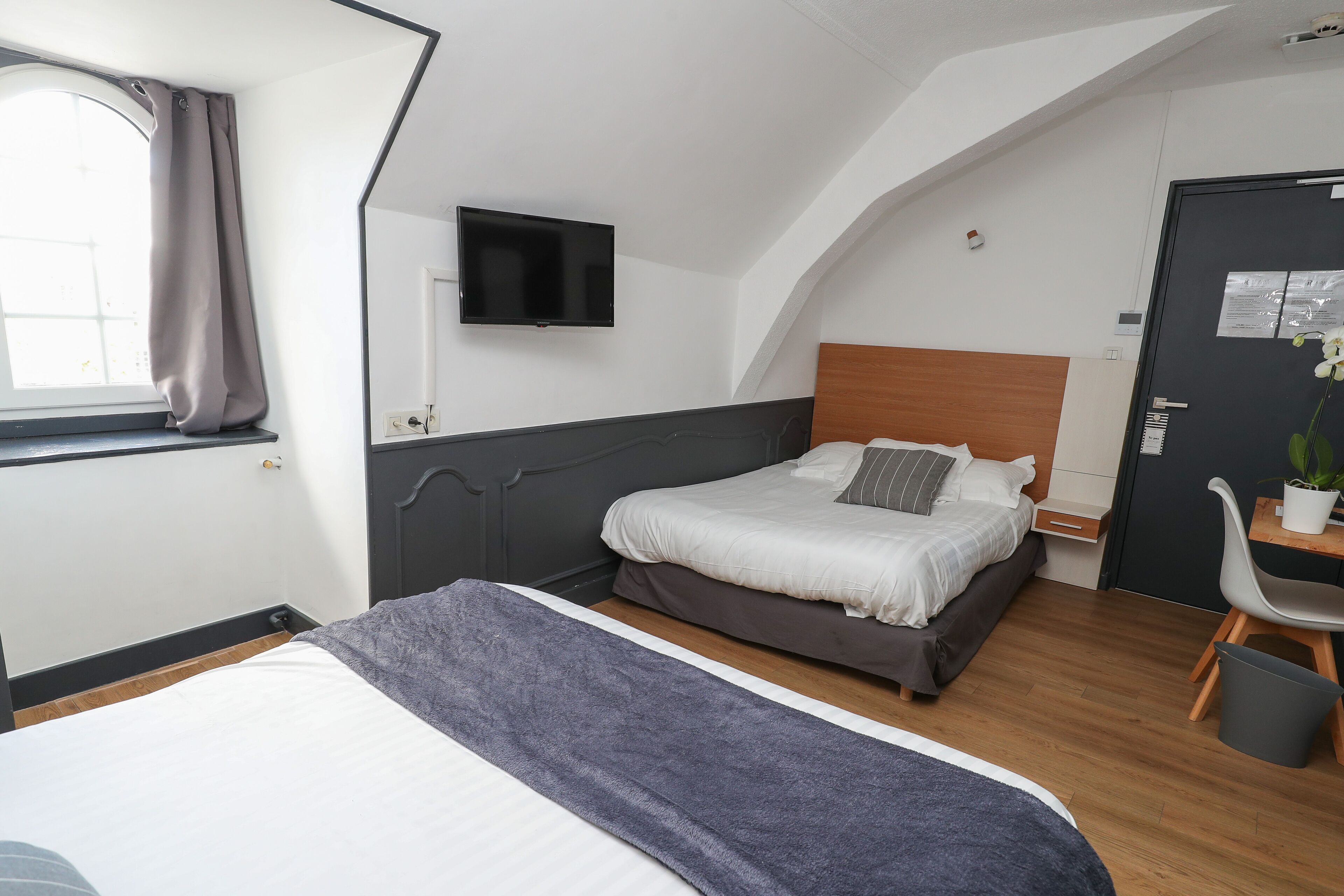 Quarto com cama, televisão na parede, escrivaninha com cadeira e janela com cortinas.