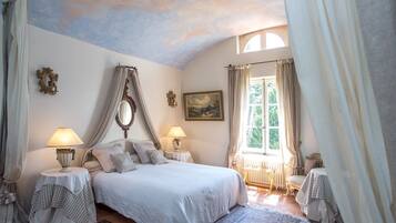 Quarto com uma cama grande, duas mesas de cabeceira, uma janela com cortinas, um mural no teto e um quadro na parede.