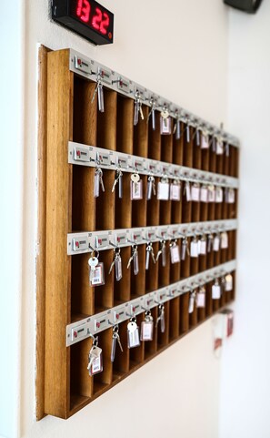 Porta-chaves fixado na parede, com compartimentos numerados, cada um contendo uma chave e uma etiqueta com nome.