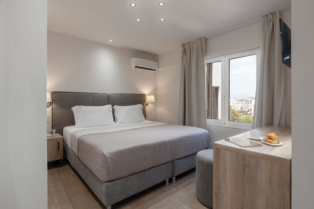Quarto de hotel moderno com uma cama, abajures, uma escrivaninha com um laptop e uma janela com cortinas.