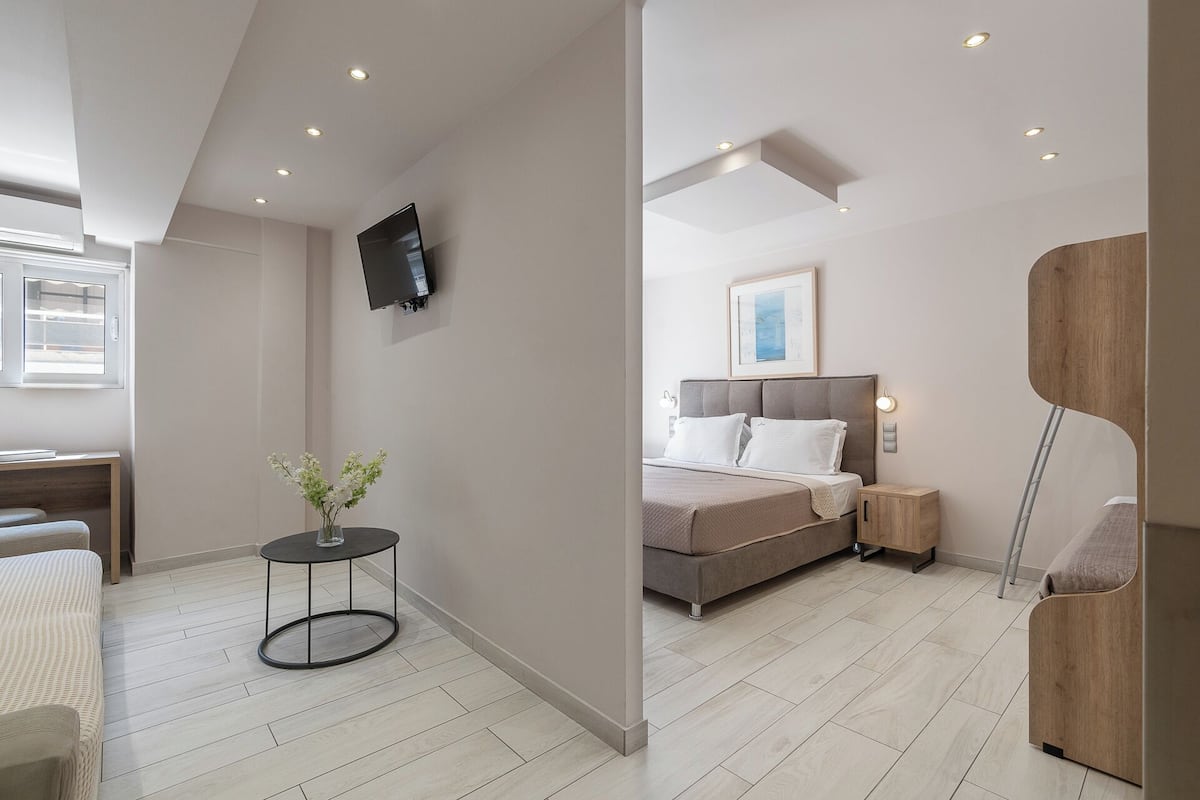 Quarto moderno com cama, mesas de cabeceira, televisão na parede e janela com persianas.
