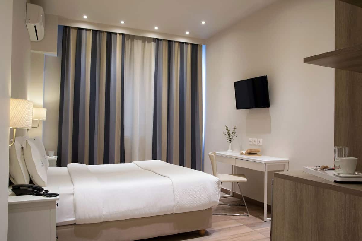Quarto de hotel com cama, escrivaninha, cadeira, televisão e telefone.