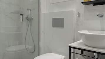 Uma casa de banho moderna com cabine de duche em vidro, sanita branca e toucador preto com lavatório branco.
