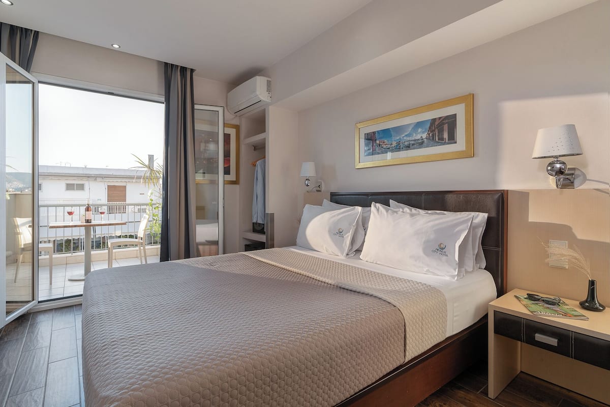 Quarto de hotel com cama, mesa de cabeceira, luminária, quadro e vista para o exterior.